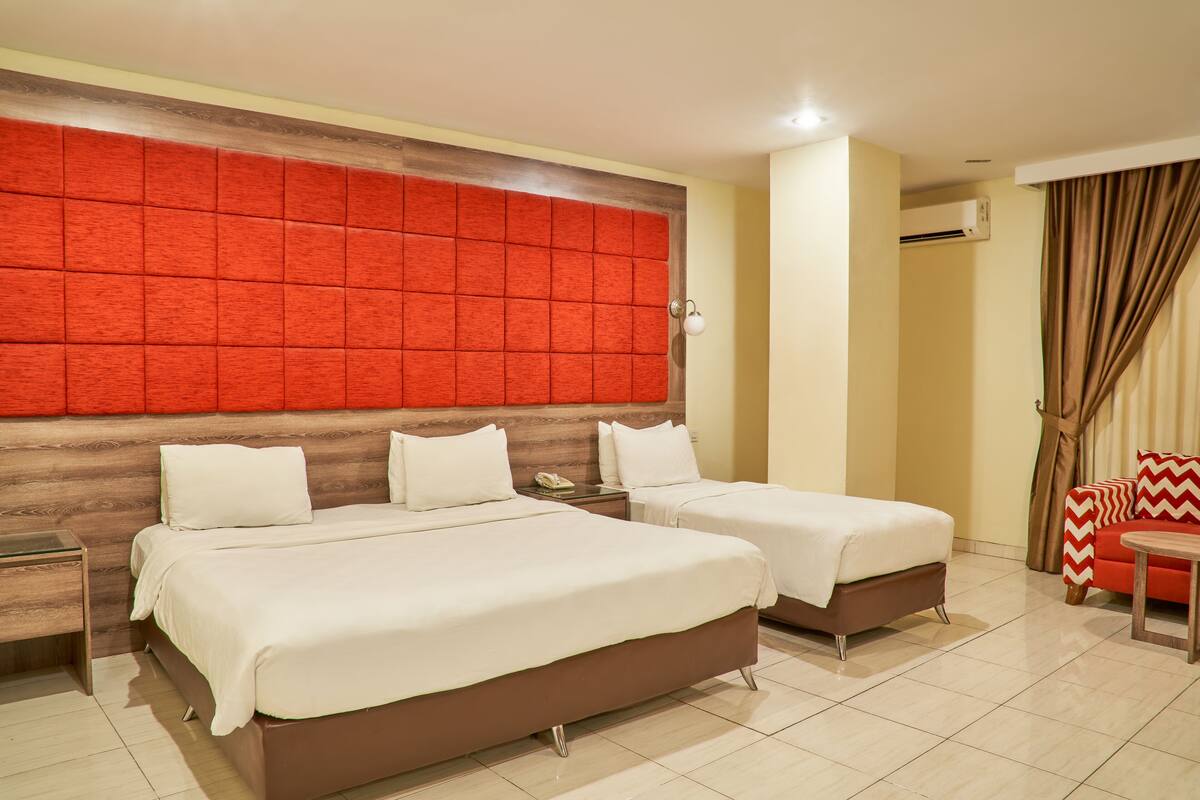Quarto de hotel com duas camas, uma parede de destaque vermelha, uma cadeira com padrão vermelho e branco em Chevron e uma mesa pequena.