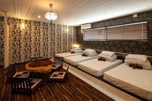 Quarto de hotel com três camas, piso de madeira, parede estampada e luminária no teto.