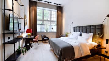 Quarto de hotel moderno com uma cama grande, uma escrivaninha com cadeira, uma estante e uma janela com cortinas.