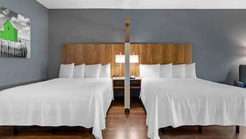 Quarto de hotel com duas camas, cabeceira de madeira, mesa de cabeceira com abajur e um quadro com um edifício verde na parede.