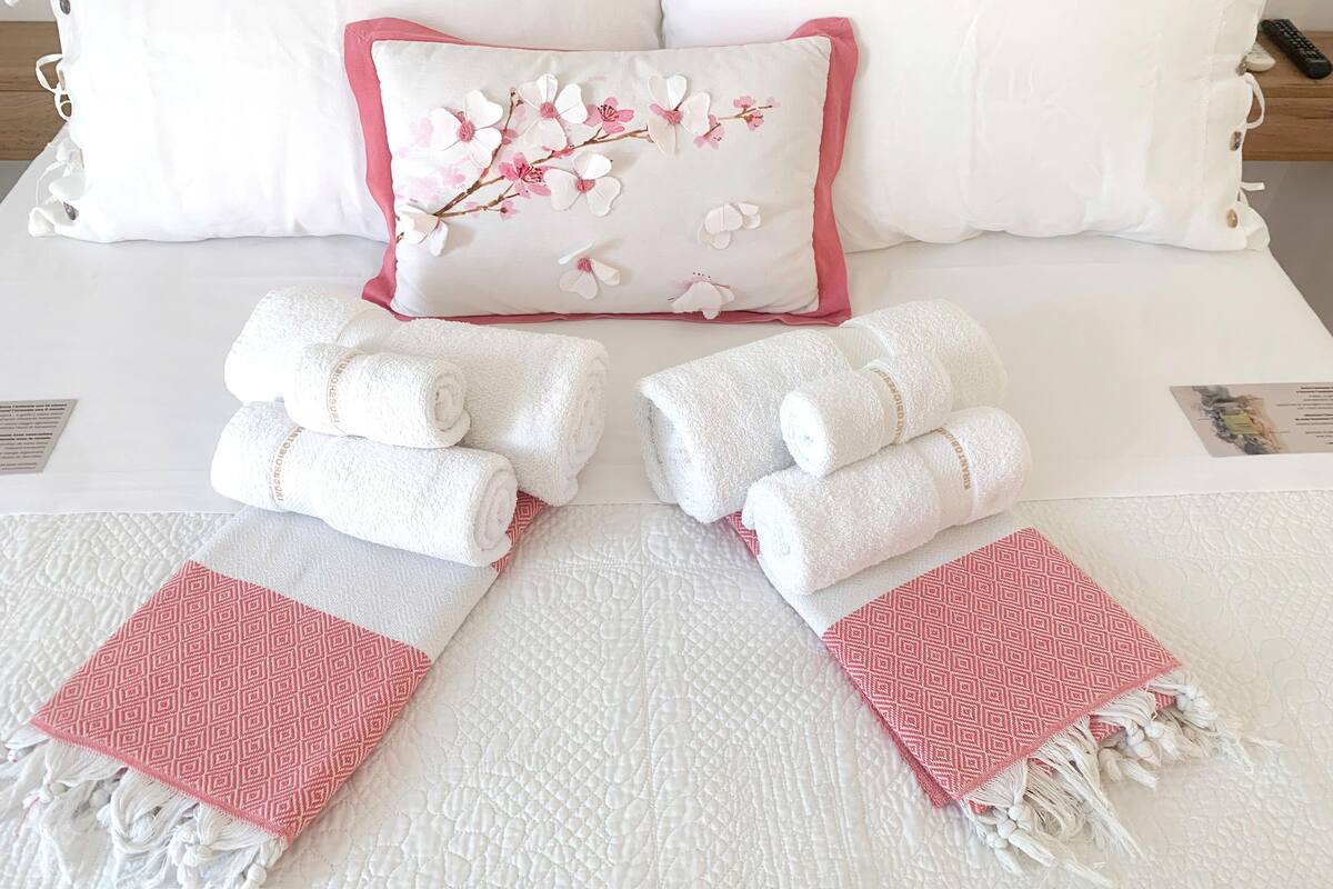 Quarto de hotel bem arrumado, com cama, almofadas, toalhas dobradas e um manta decorativa.
