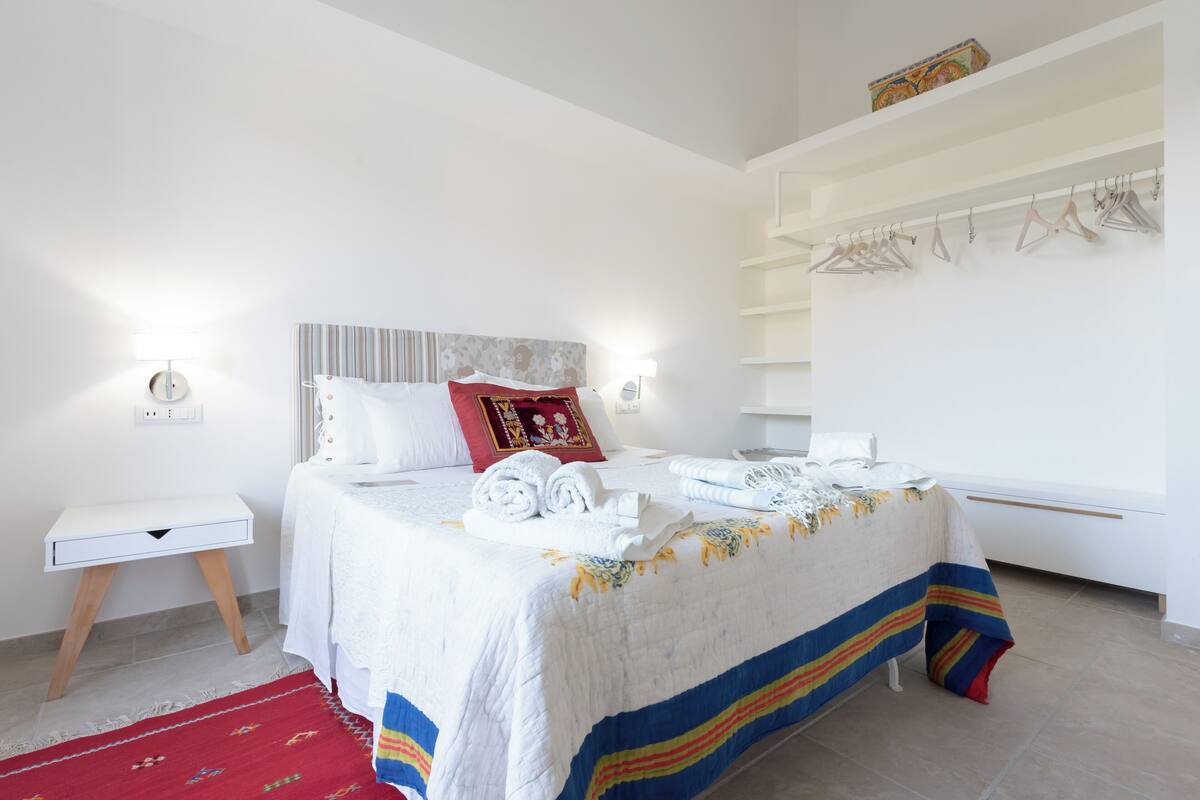 Quarto bem arrumado com cama, mesas de cabeceira e um cabideiro.