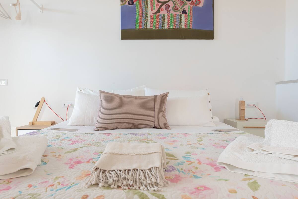 Cama bem arrumada com colcha florida, travesseiros brancos e manta dobrada.