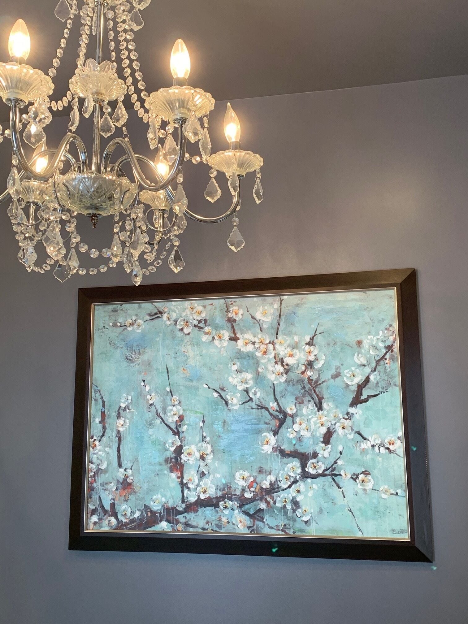 Um candelabro com várias luzes e um quadro de uma árvore florida na parede.