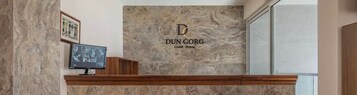 Uma receção com um monitor, uma parede de pedra com o logotipo "DUN GORG Guest House" e um balcão de madeira.