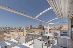 Terraço no telhado com mesas e cadeiras, oferecendo vista para o horizonte urbano com uma cúpula imponente e edifícios.