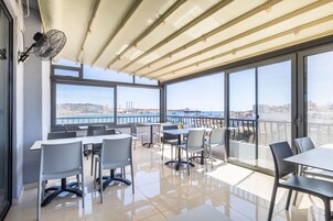 Uma sala de conferências moderna com janelas amplas, um ventilador e vista para a cidade e o mar.