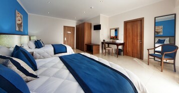 Quarto de hotel com duas camas, uma escrivaninha, uma cadeira e uma televisão.