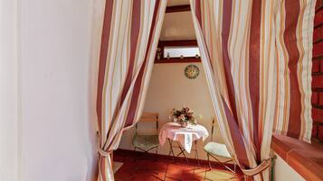 Um quarto com uma pequena mesa e cadeira, uma janela com cortinas e uma parede de tijolos.