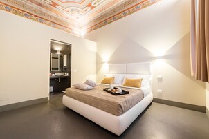 Quarto de hotel moderno com uma cama grande, banheiro com espelho e teto decorativo.
