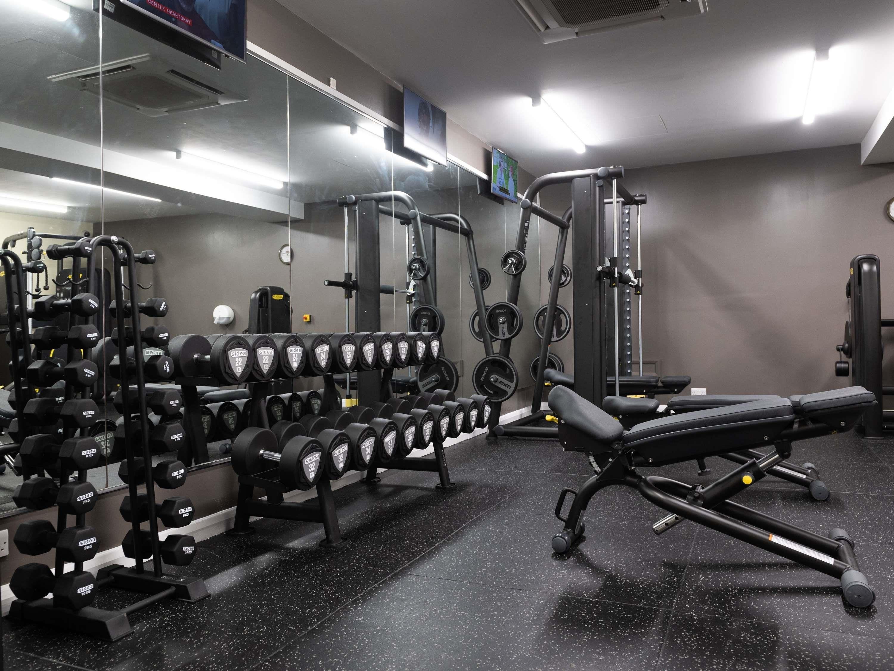 Academia com equipamentos de musculação, um banco e um espelho.