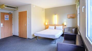 Quarto de hotel com cama, escrivaninha, cadeira, janela e porta.