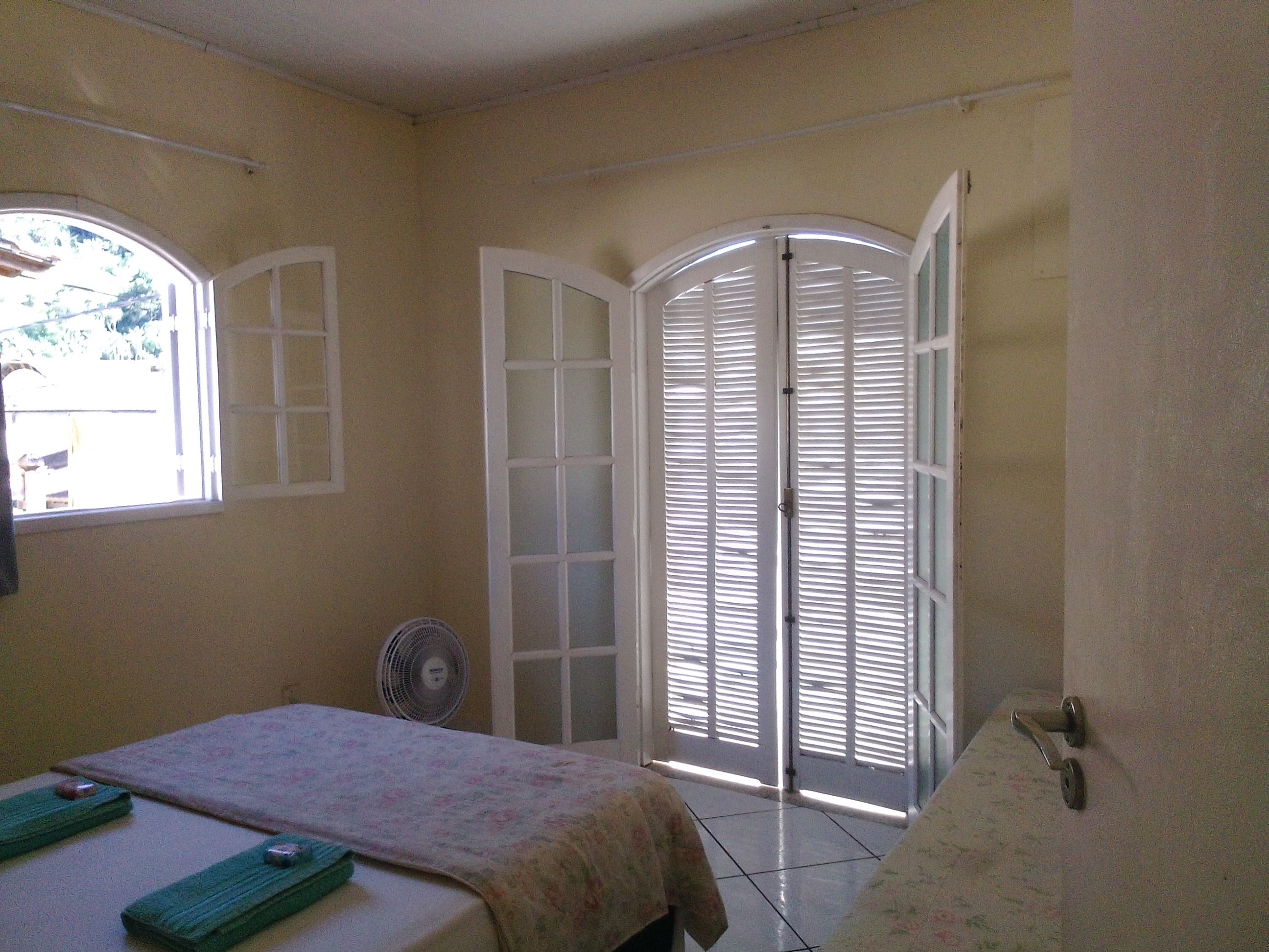Quarto com cama, ventilador e janela.