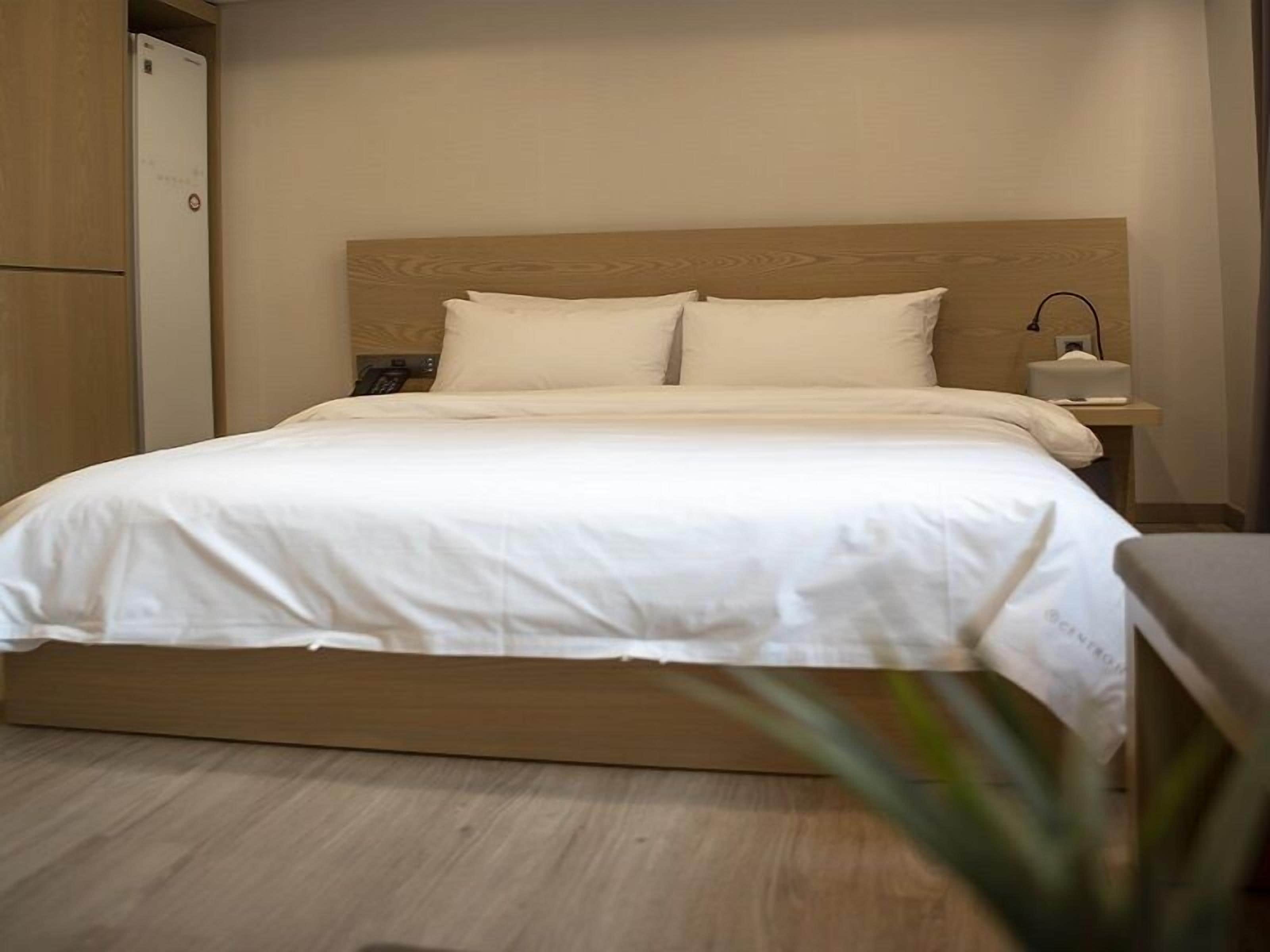Cama bem arrumada com lençóis brancos em quarto com piso de madeira e cabeceira de madeira.
