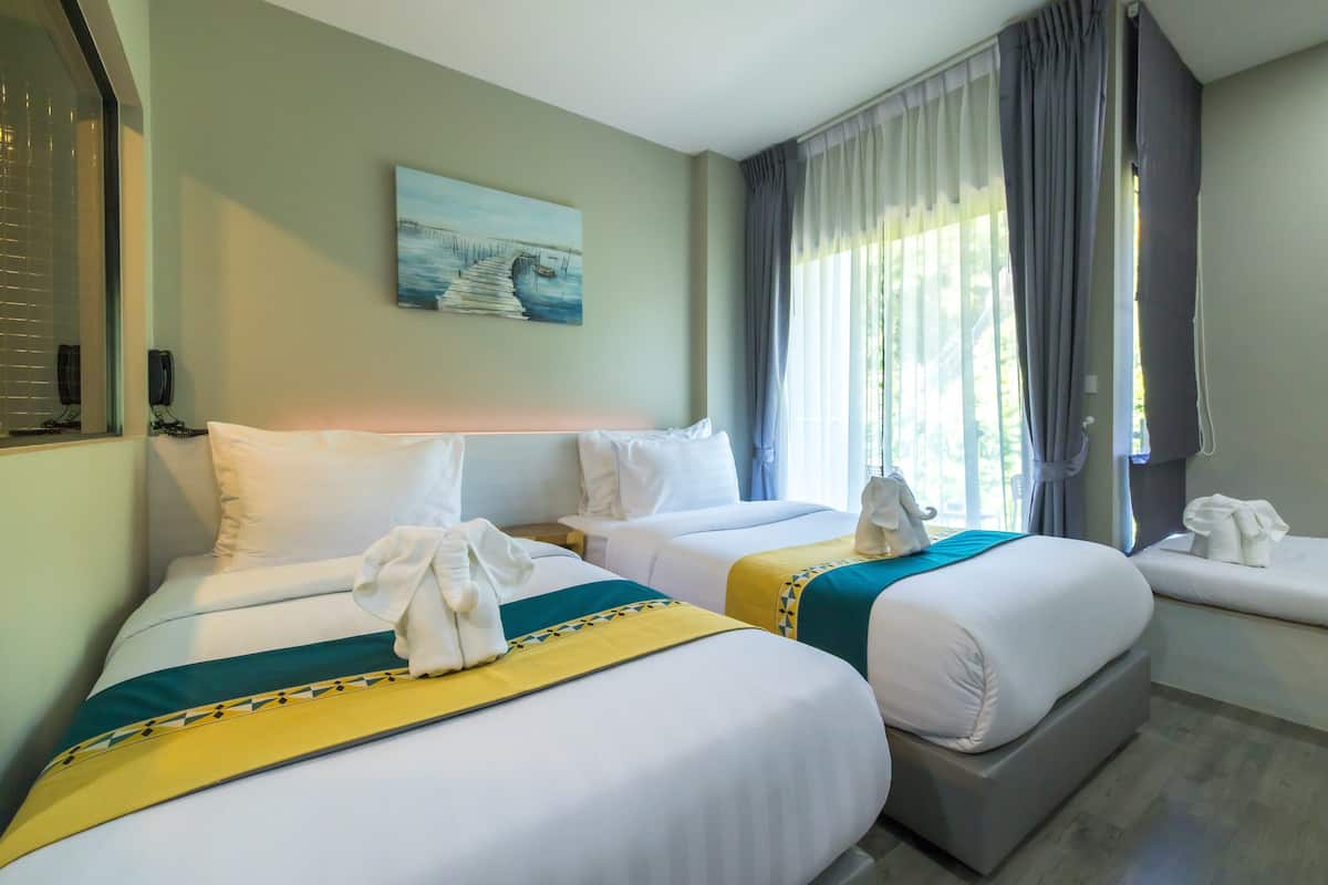 Quarto de hotel com duas camas, um quadro na parede e uma janela com cortinas.