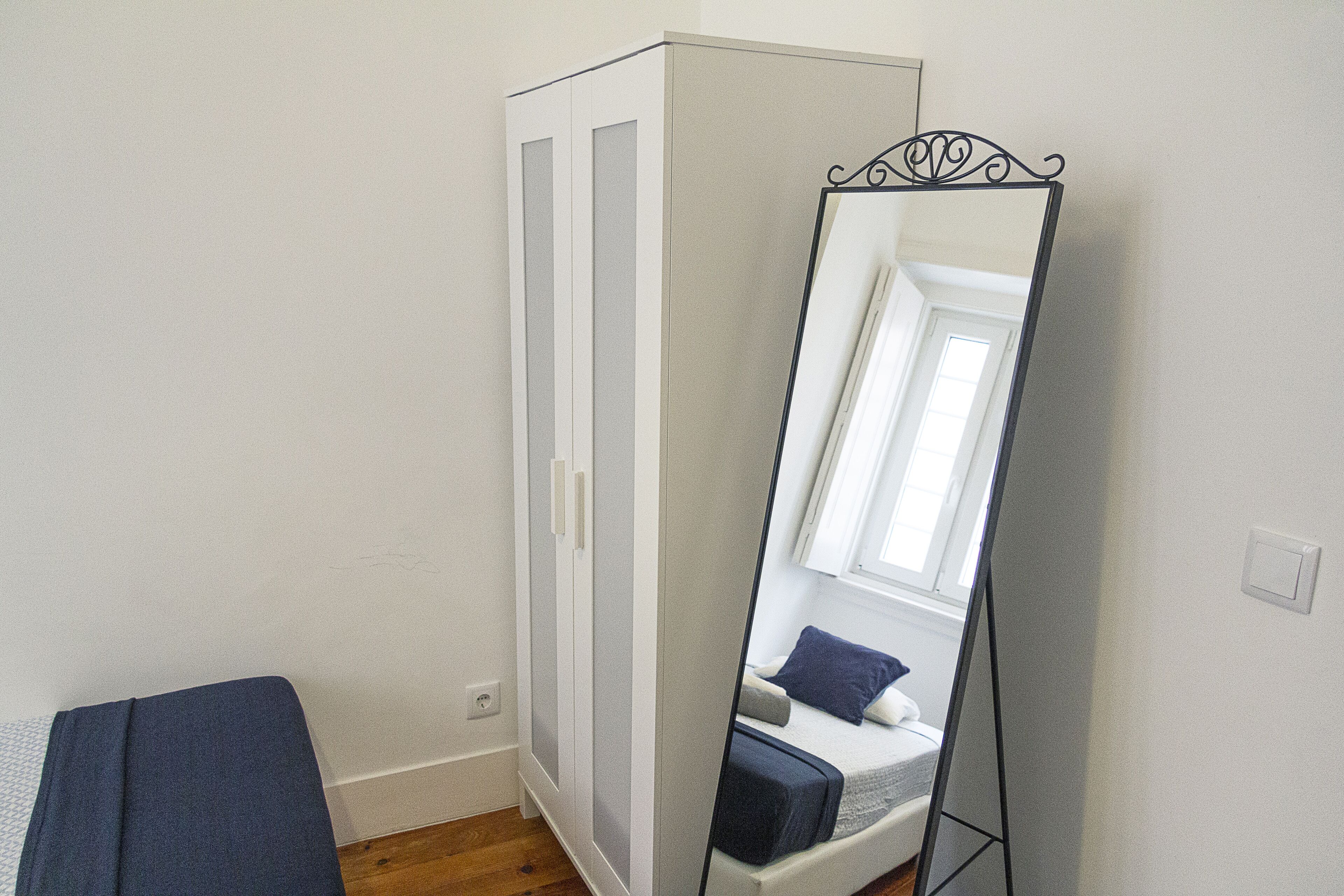 Quarto com guarda-roupa, cama e espelho de corpo inteiro.