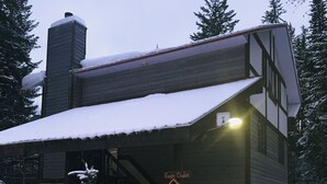 Uma pousada de dois andares com telhado coberto de neve e uma placa com a inscrição 'Eagle Chalet'.