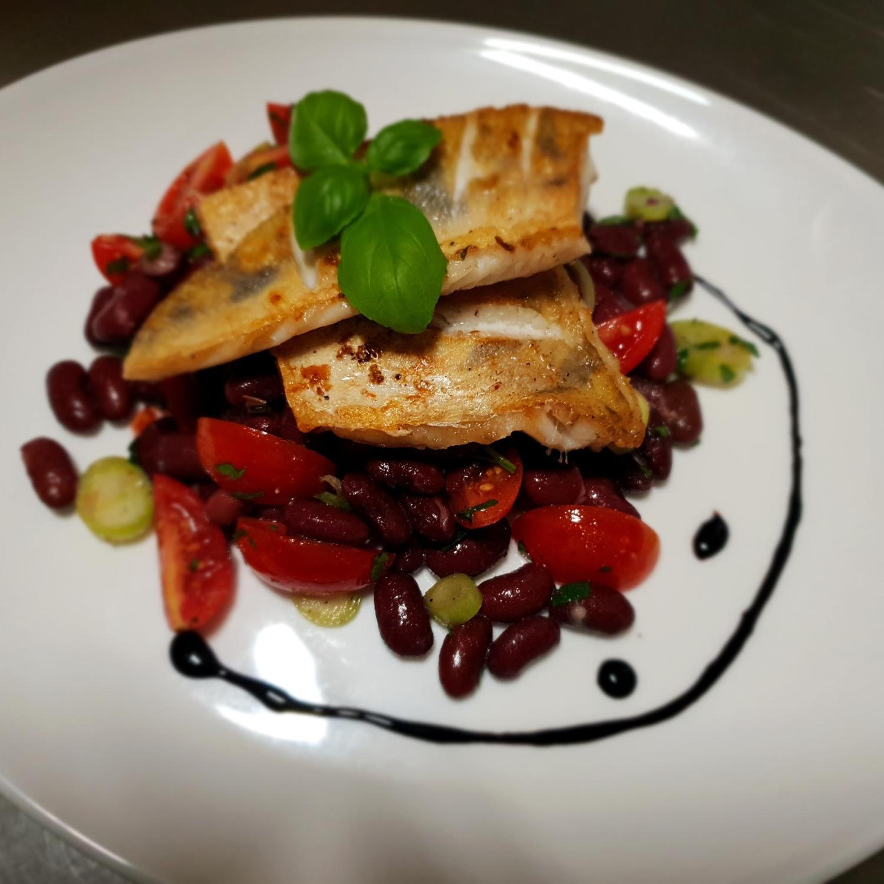 Prato com peixe grelhado, feijão vermelho, tomate cereja e um guarnição de manjericão.
