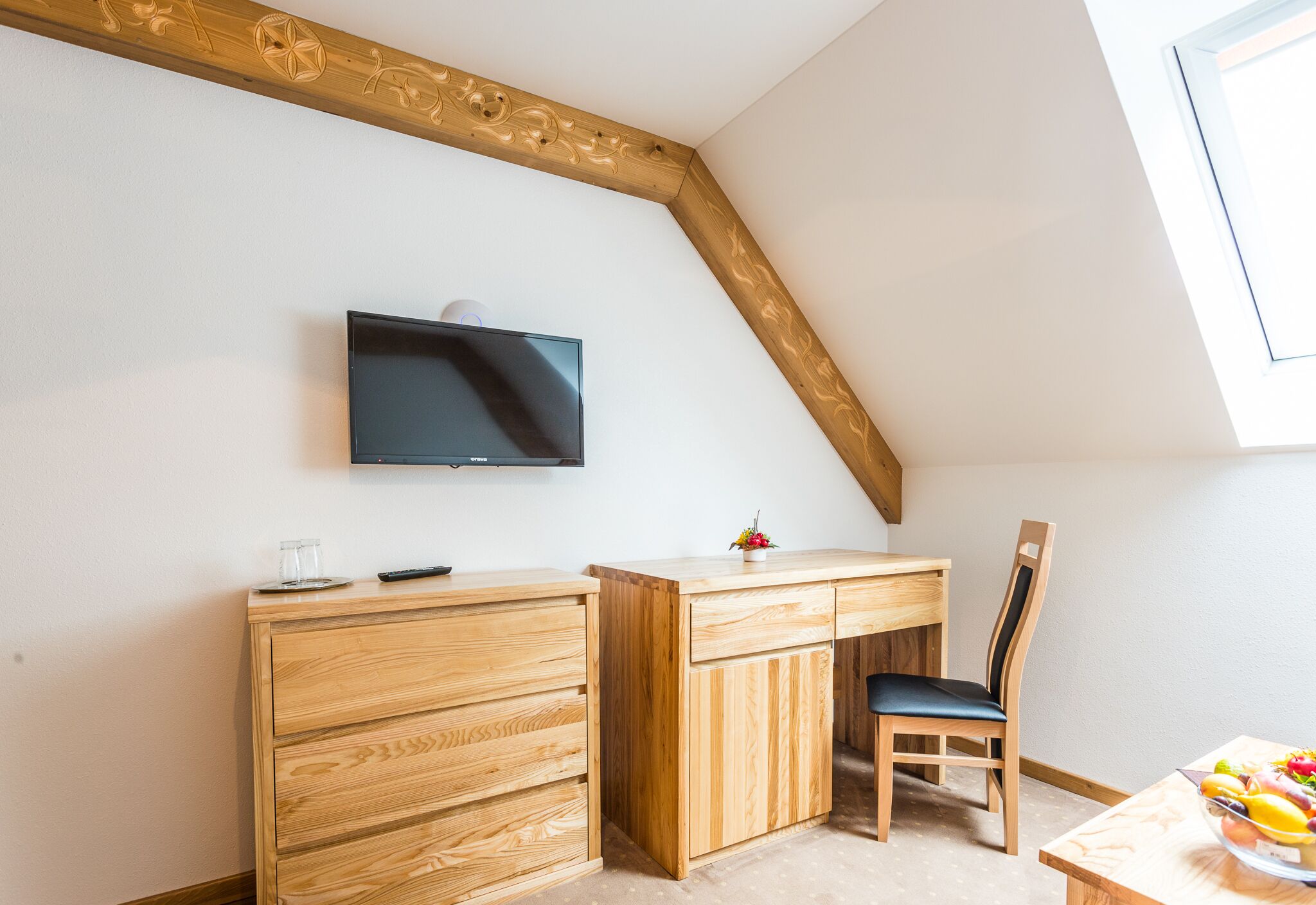 Quarto com escrivaninha de madeira, uma cadeira, televisão na parede e uma janela.