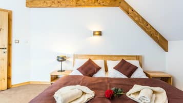Quarto com teto inclinado, cabeceira de madeira, duas mesas de cabeceira, uma luminária, cama com duas almofadas e toalhas sobre a cama.