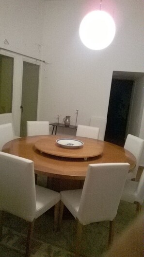 Mesa redonda de madeira com cadeiras brancas, um pequeno prato decorativo e uma luz pendente brilhante.