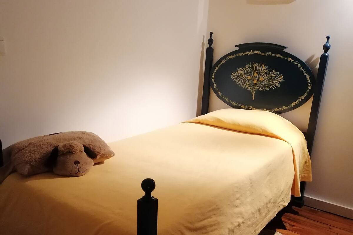 Uma cama com cabeceira, um urso de pelúcia e uma foto emoldurada na parede.