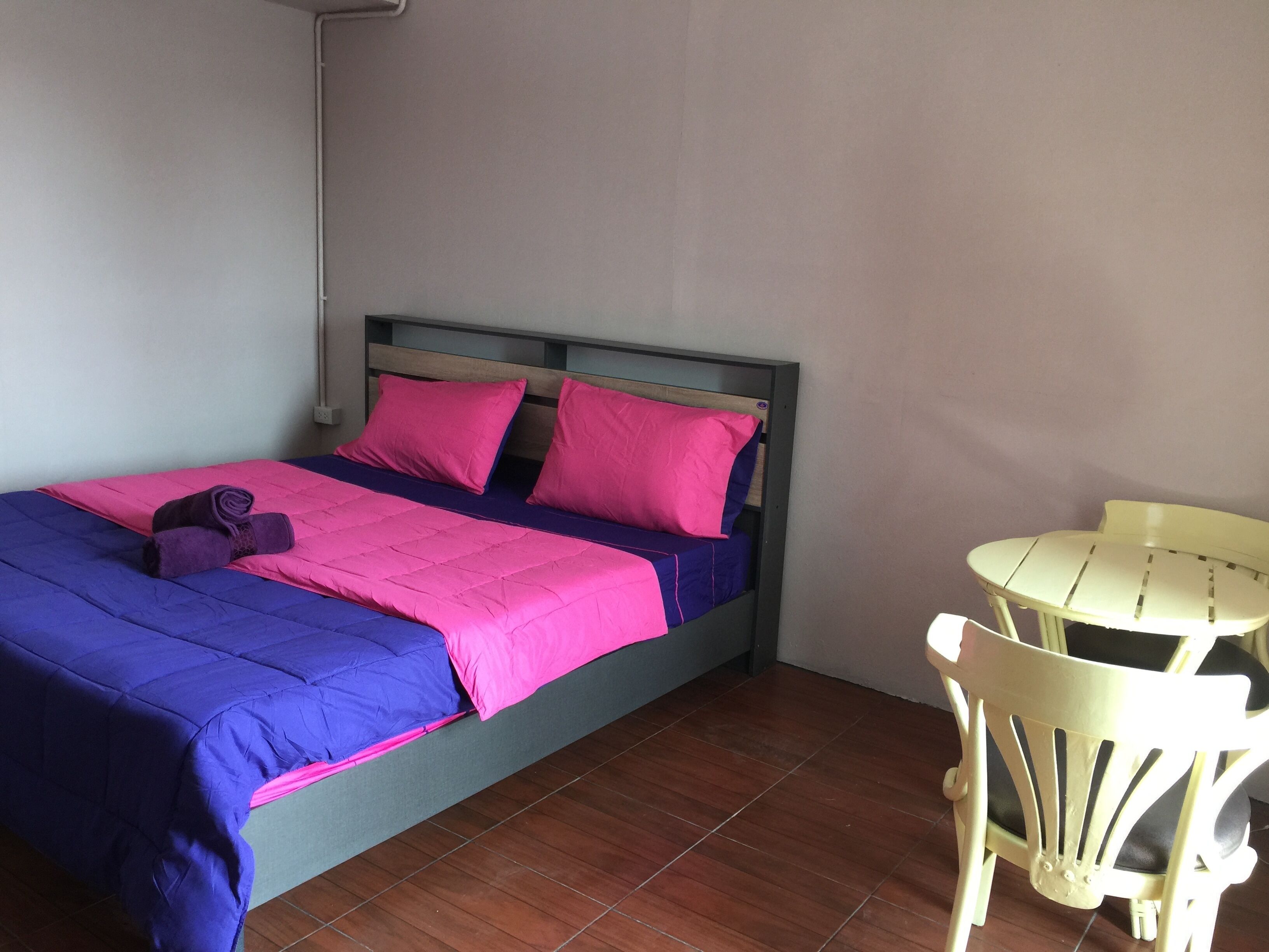 Uma cama de solteiro com cabeceira de madeira, uma mesa com uma cadeira e piso de azulejos.