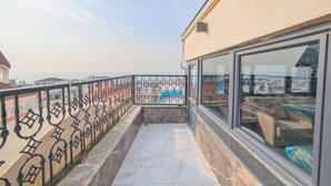 Uma varanda com guarda-corpo estampado, chão de azulejos e vista para a paisagem urbana.