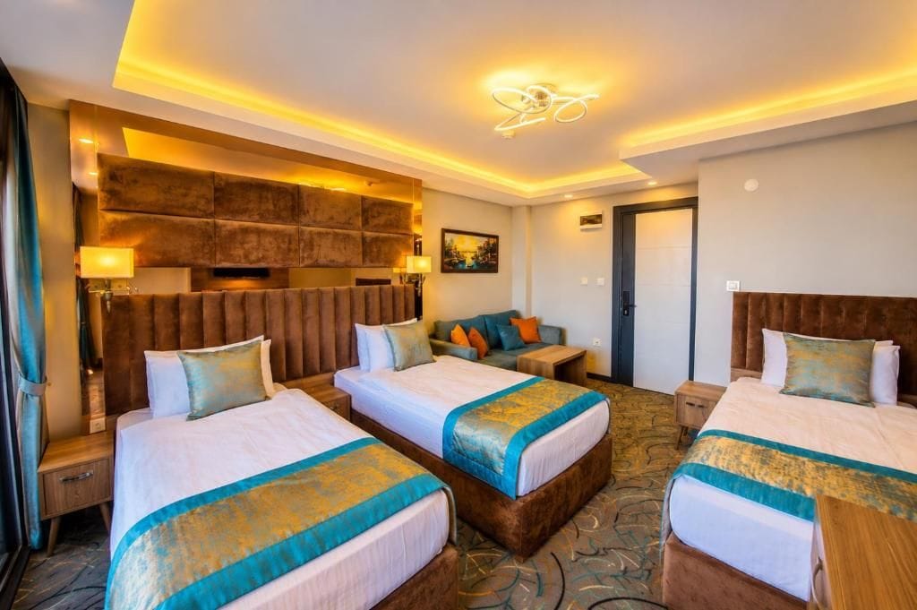 Quarto de hotel com duas camas, um sofá, uma mesa de trabalho e cabeceira com televisão integrada.