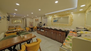 Uma sala de jantar com várias mesas e cadeiras, um buffet com diversos pratos, e espelhos decorativos na parede.