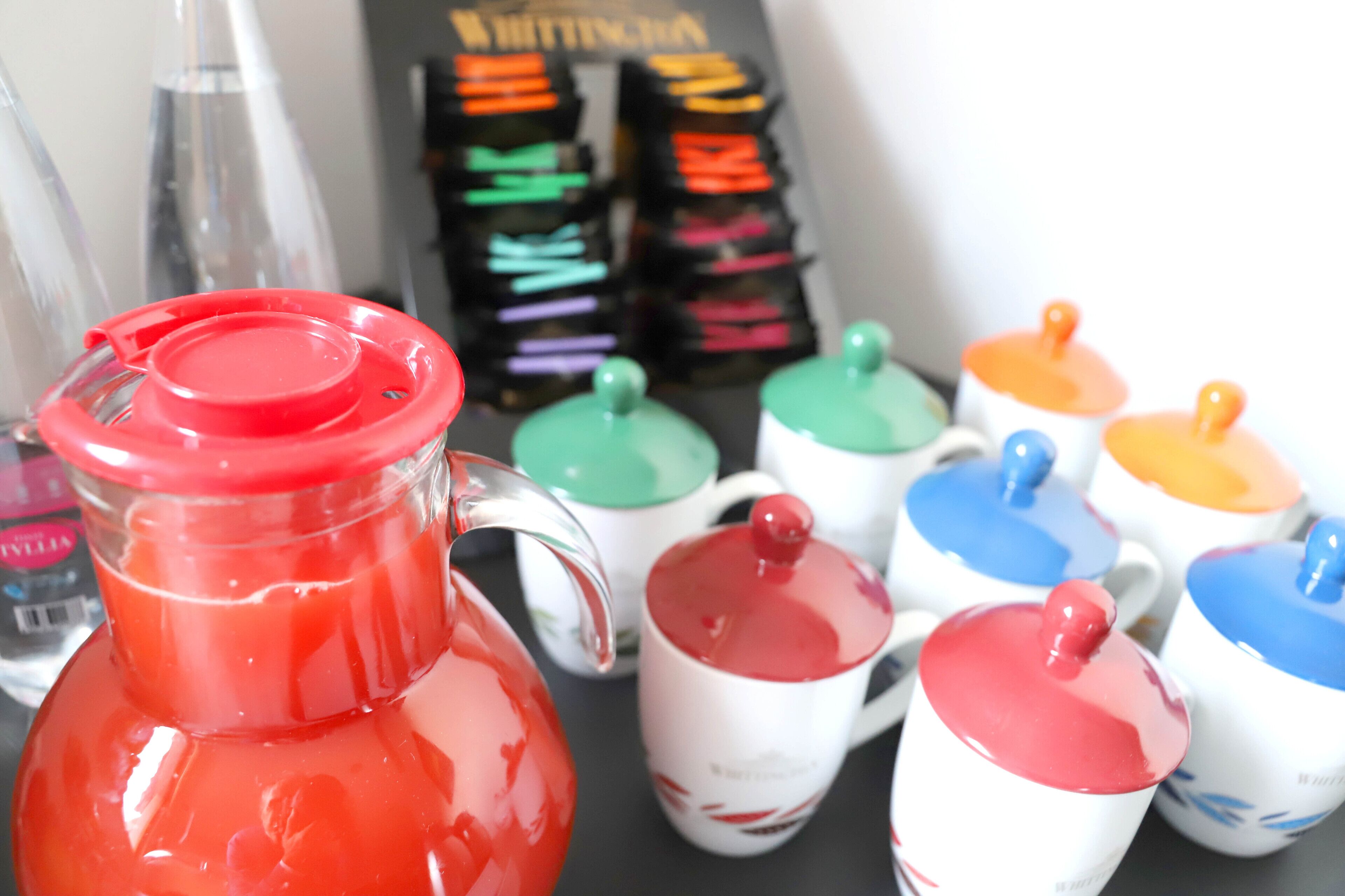 Diversos recipientes coloridos e um jarro de vidro vermelho sobre uma mesa.