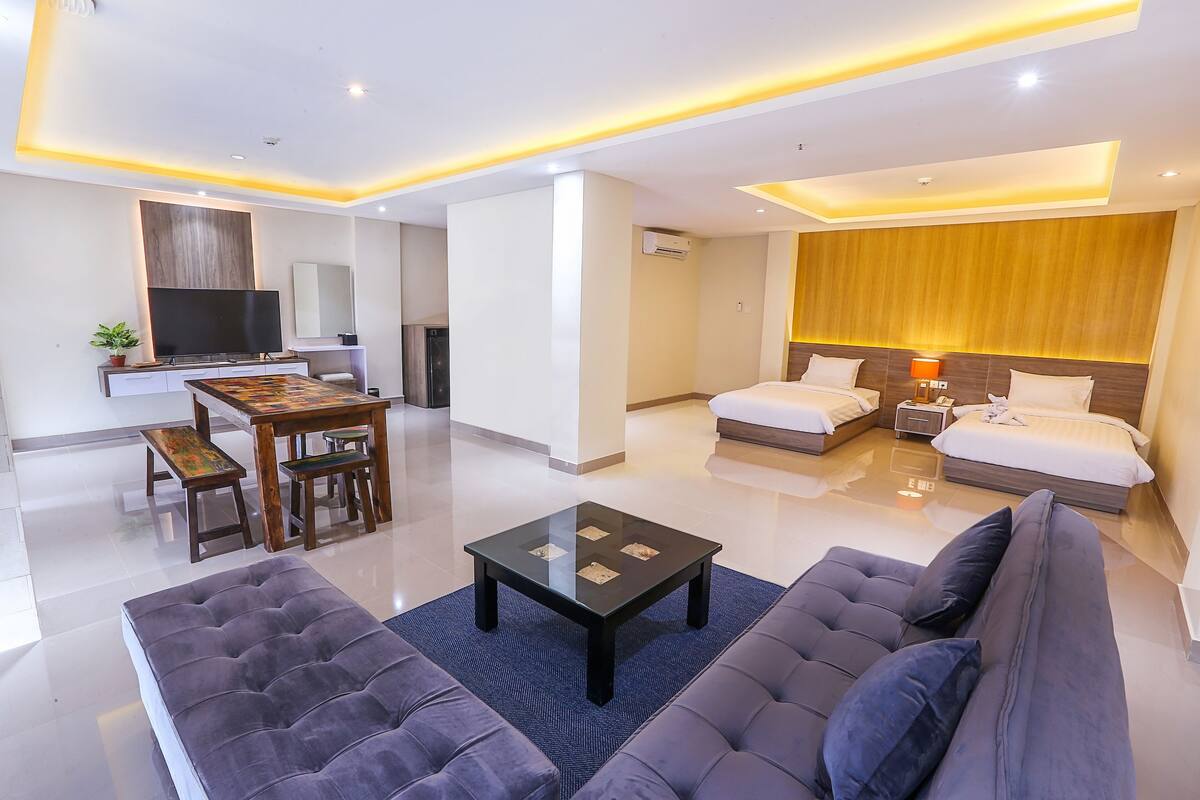 Quarto de hotel moderno com área de estar, mesa de jantar e quarto com uma cama grande e mesa de cabeceira.