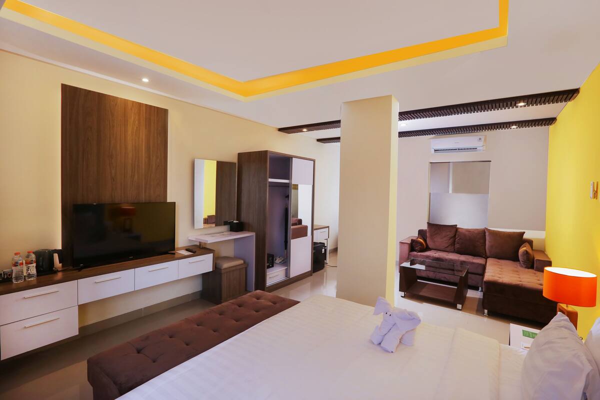 Quarto de hotel moderno com uma cama grande, televisão, guarda-roupa, área de estar e sofá.