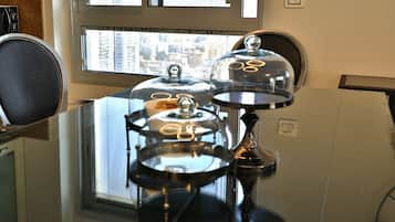 Uma vitrine com tampo de vidro exibindo três objetos cobertos, uma cadeira e uma janela com persianas.