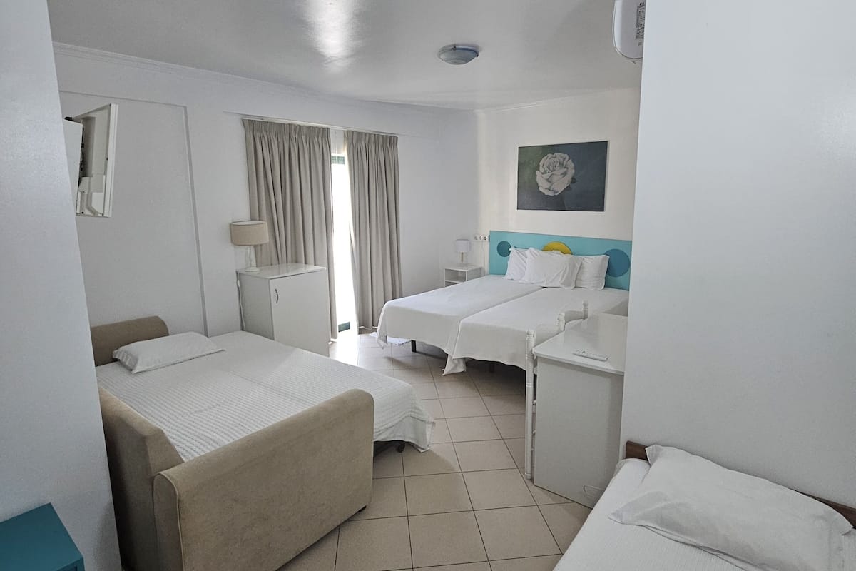 Quarto de hotel com duas camas, uma mesa pequena, um espelho e uma janela com cortinas.