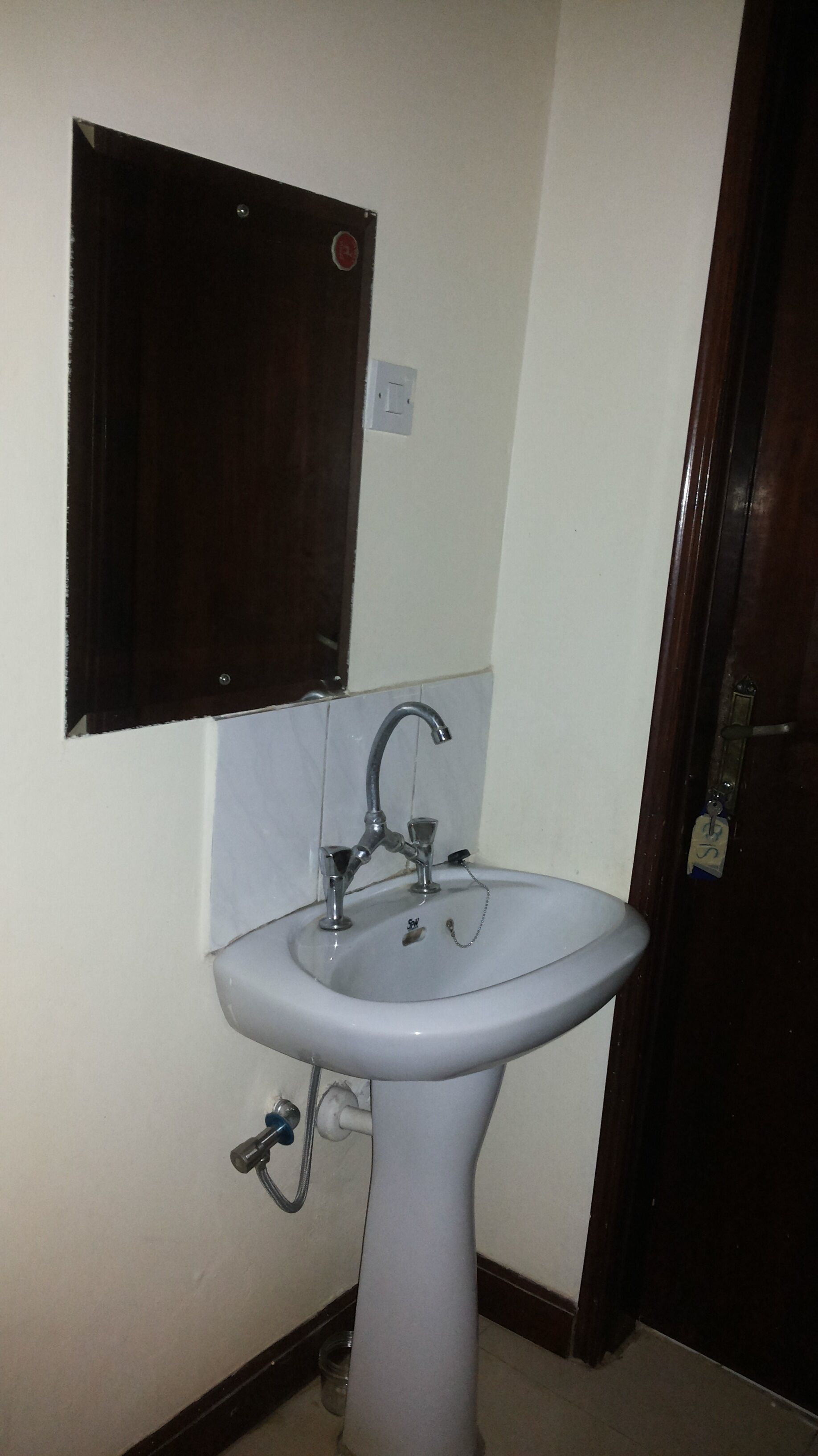 Casa de banho com lavatório pedestal branco, espelho em cima e porta à direita.