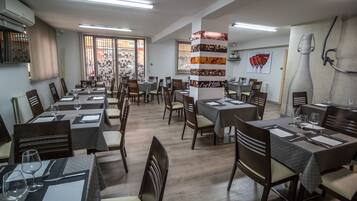 Um restaurante com várias mesas e cadeiras, dispostas num espaço amplo, com um pilar central com um design colorido.