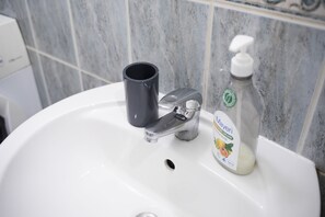 Uma pia de banheiro com uma torneira, um dispensador de sabão e uma xícara.