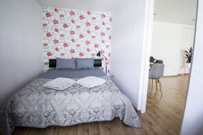 Quarto com papel de parede floral, colcha de cama estampada em cinza e piso de madeira.