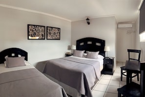 Quarto de hotel com duas camas, uma mesa de cabeceira com abajur, uma cadeira e uma obra de arte na parede.