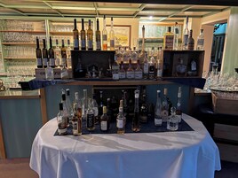 Uma área de bar com prateleiras de garrafas de vinho e copos, uma mesa com garrafas e um comedouro decorativo.