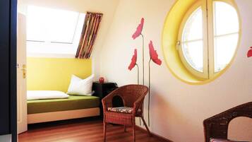 Quarto com cama, cadeira, mesa pequena, janela e parede com janela circular.