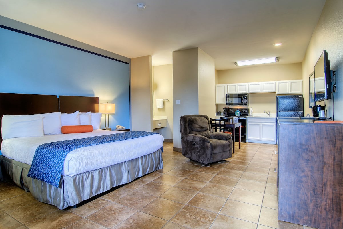 Quarto de hotel com cama, cadeira, escrivaninha e cozinha compacta.