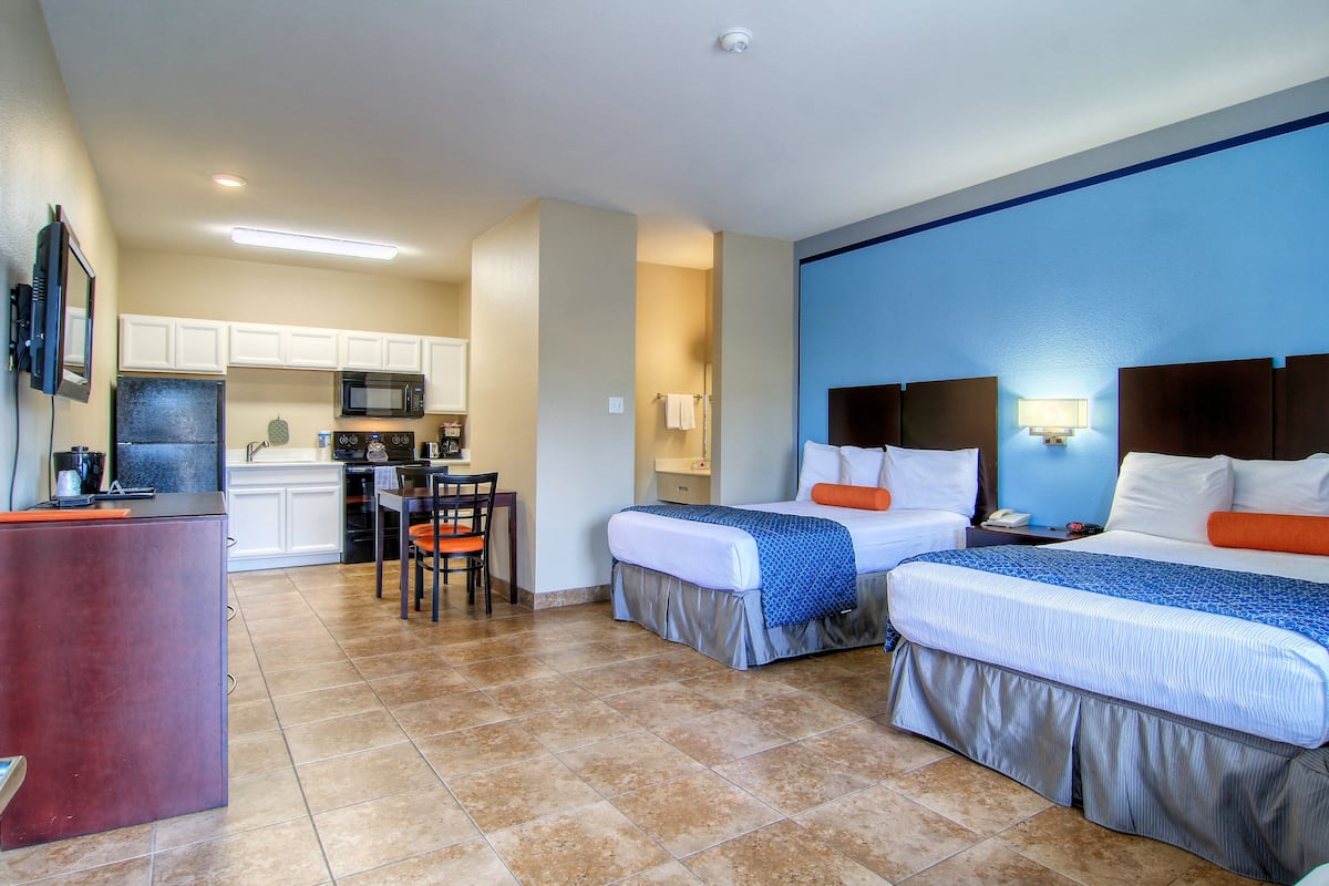 Quarto de hotel com duas camas, cozinha compacta, mesa de trabalho e banheiro.