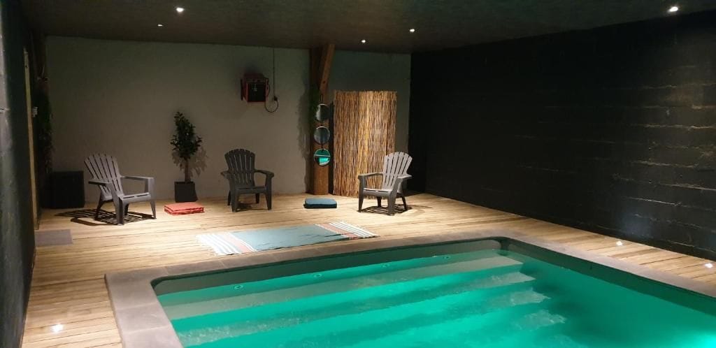 Área de piscina com piso de madeira, duas cadeiras e uma mesa pequena.