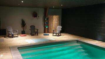 Área de piscina com piso de madeira, duas cadeiras e uma mesa pequena.