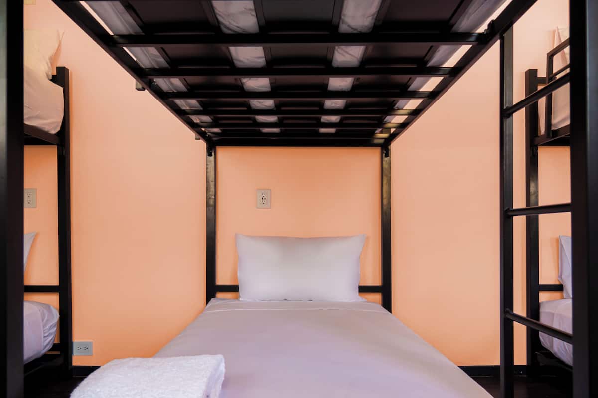 Quarto com beliche, uma cama de solteiro, um travesseiro branco e uma toalha branca no chão.