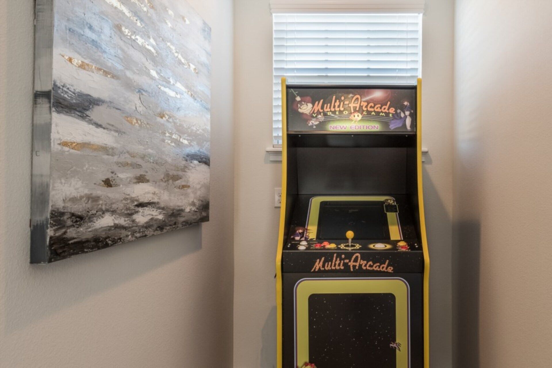 Máquina de jogos Multi Arcade num corredor com um grande quadro abstrato na parede.