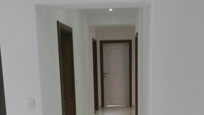 Um corredor com paredes brancas e chão de azulejos brilhantes, que leva a uma porta no final.