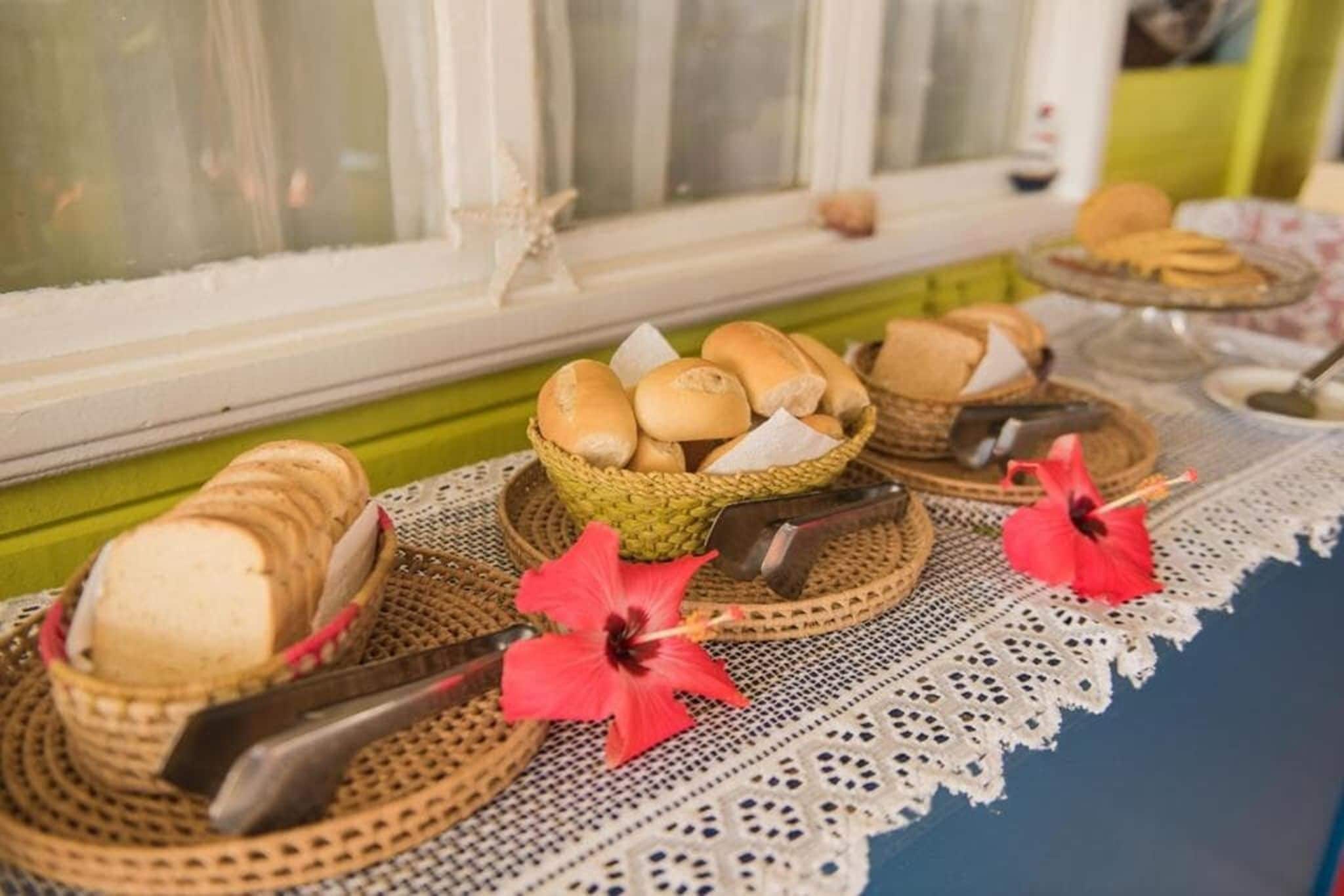 Mesa com pão, flores, uma janela e toalha de renda.